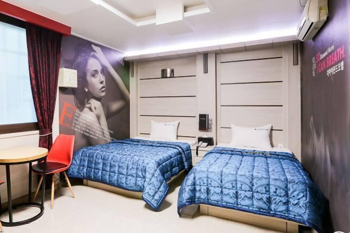 Quarto de hotel com duas camas, uma mesinha, uma cadeira e um pôster grande na parede.