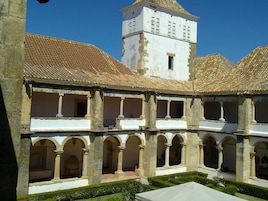 Um pátio com uma torre central, rodeado por arcos e um telhado em azulejos.