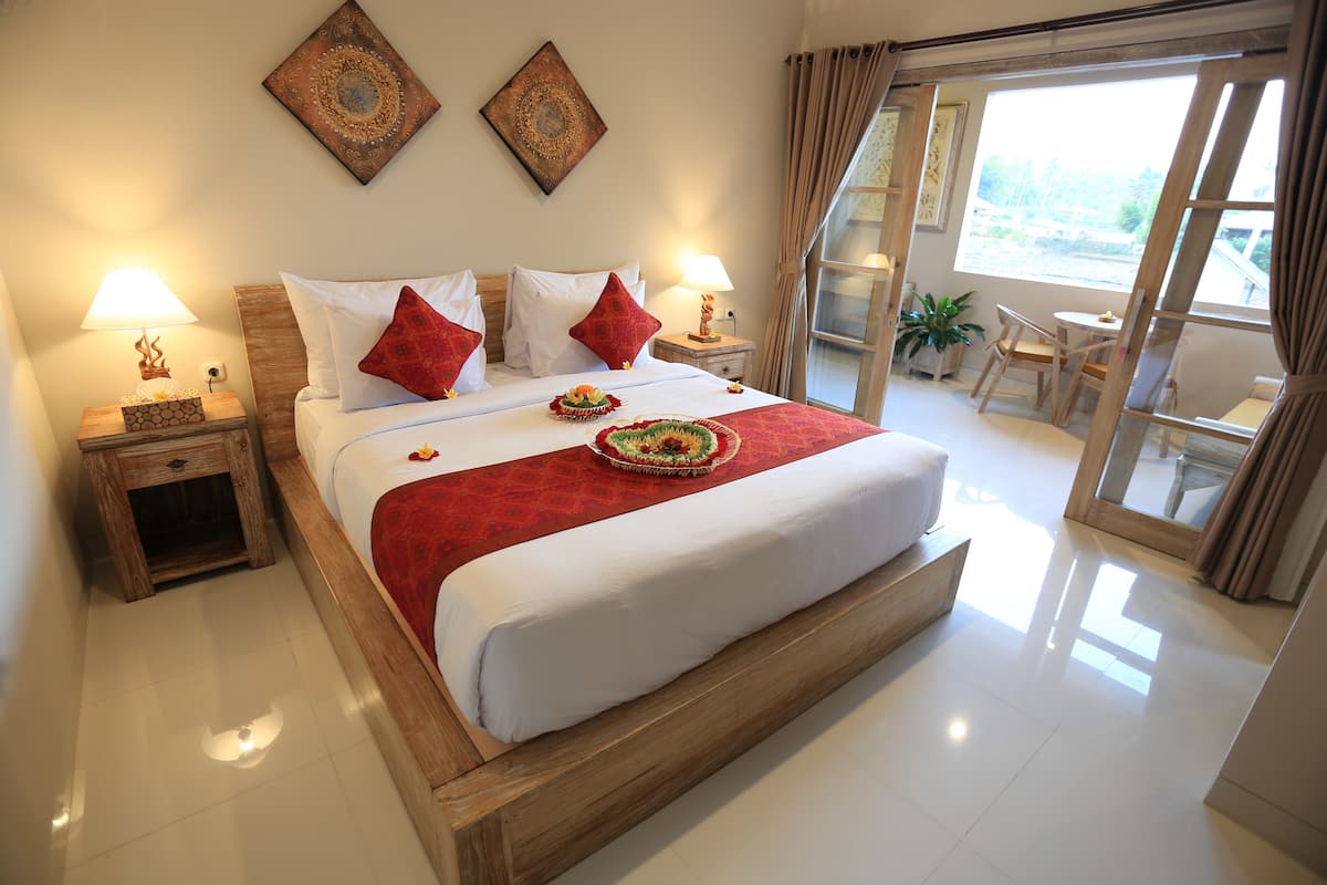 Quarto espaçoso com uma cama grande, duas mesas de cabeceira, uma varanda com mesa e cadeiras, e vista para o exterior.
