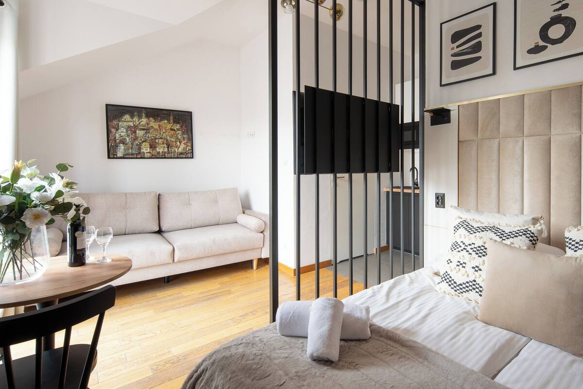 Quarto moderno com cama, sofá, mesa de jantar com um vaso de flores e um quadro na parede.