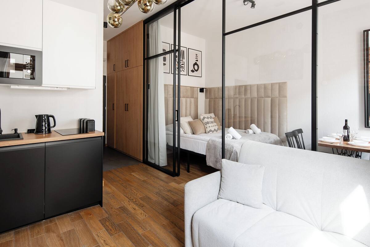 Quarto de hotel moderno com cozinha compacta, uma cama com encosto e área de jantar com mesa posta para dois.