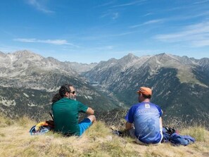 Duas pessoas sentadas numa colina gramada com vista para uma paisagem montanhosa.