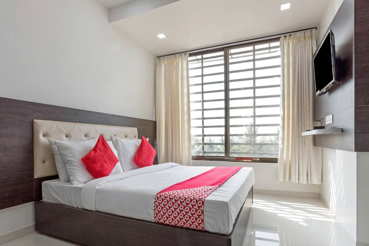 Quarto de hotel moderno com cama grande, TV de tela plana na parede e janela com cortinas.