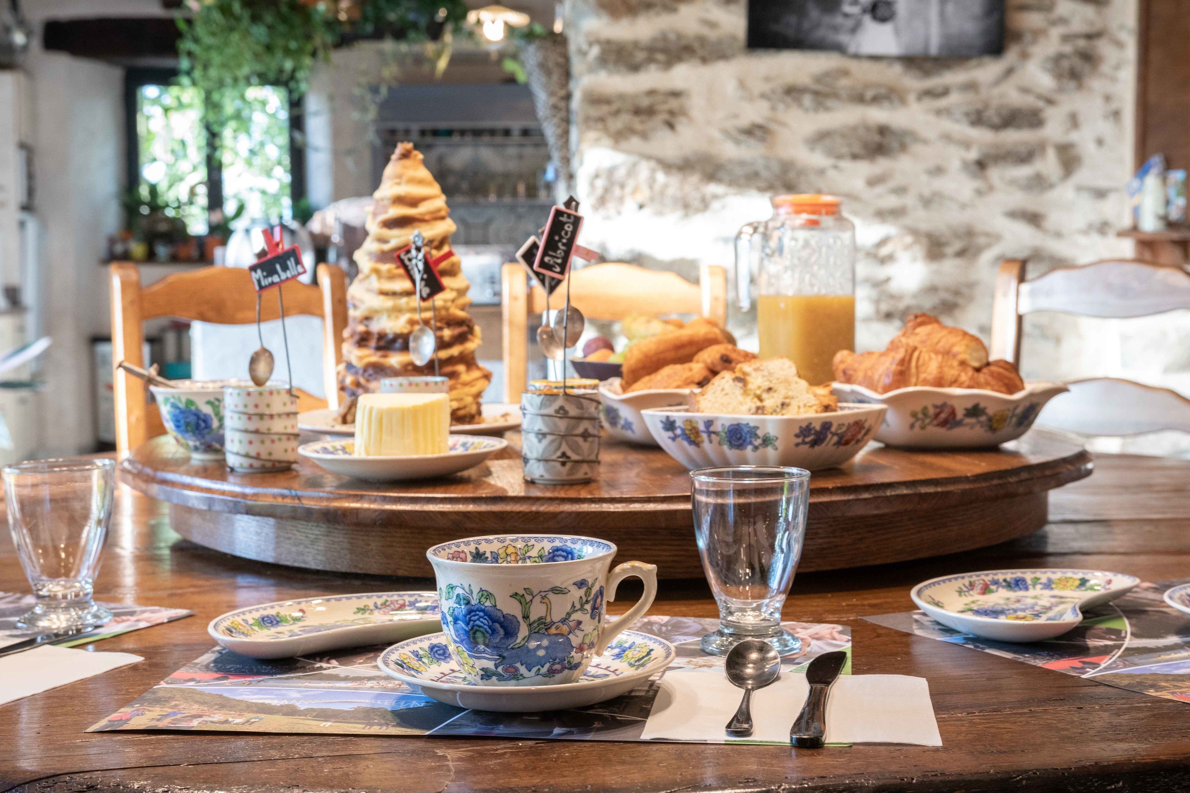 Uma mesa de café da manhã com diversos doces, uma cafeteira e uma saladeira de frutas.