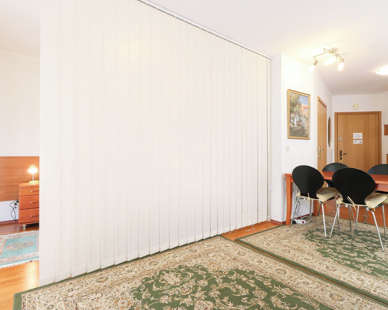 Um quarto com uma grande porta deslizante branca, uma mesa de jantar com cadeiras, um aparador de madeira e um tapete estampado.