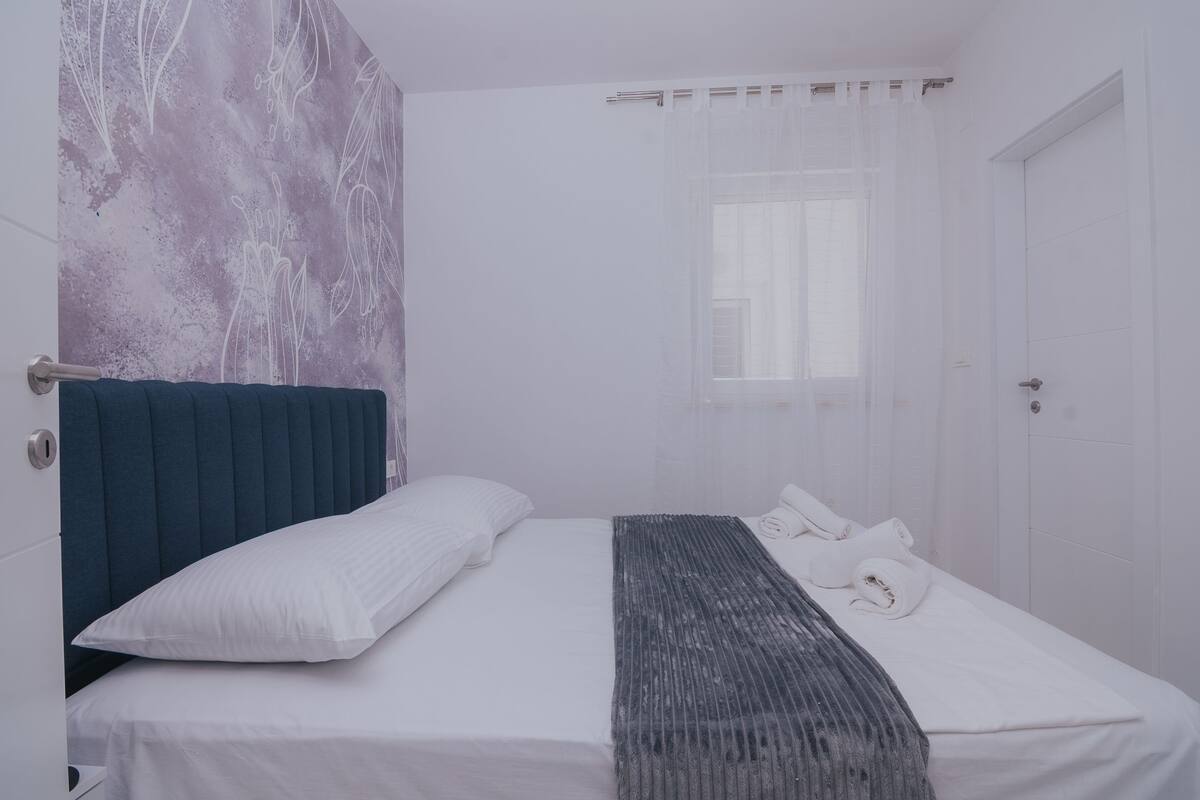 Quarto de hotel com cama, janela com cortinas leves e porta.