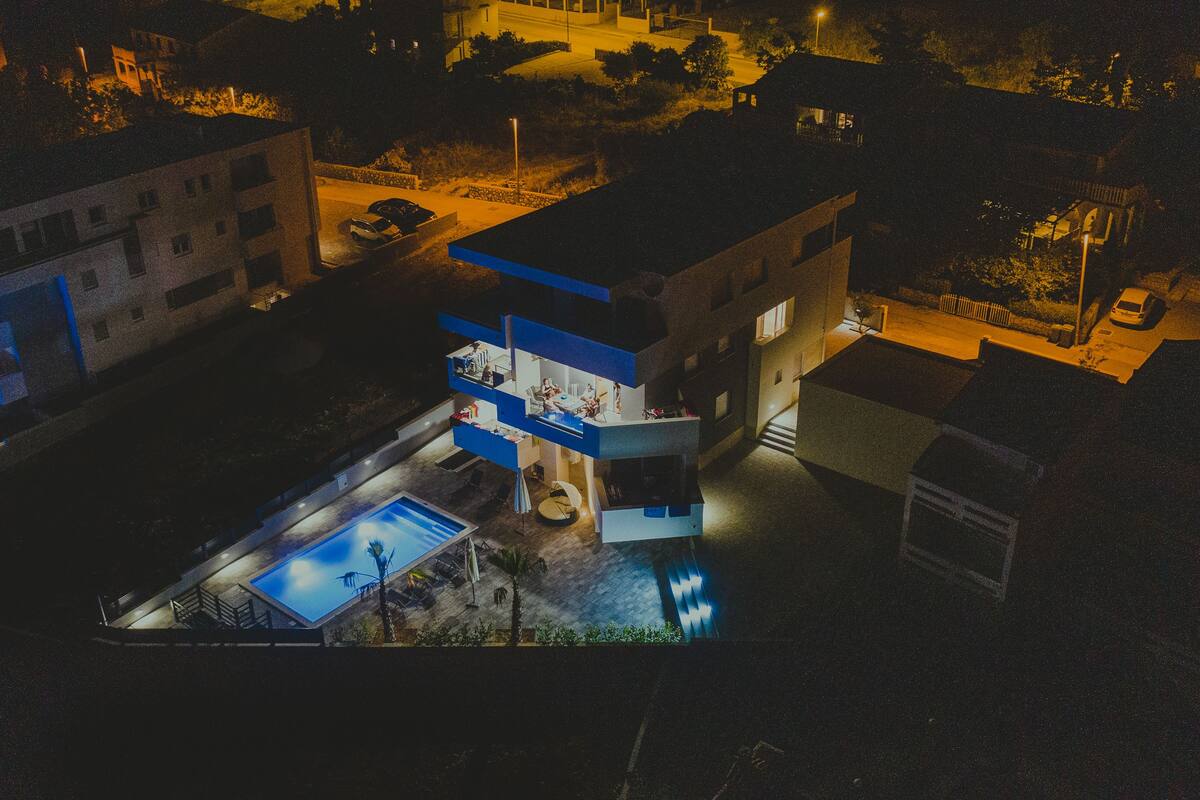 Um edifício moderno com piscina no terraço, várias varandas e fachada bem iluminada.