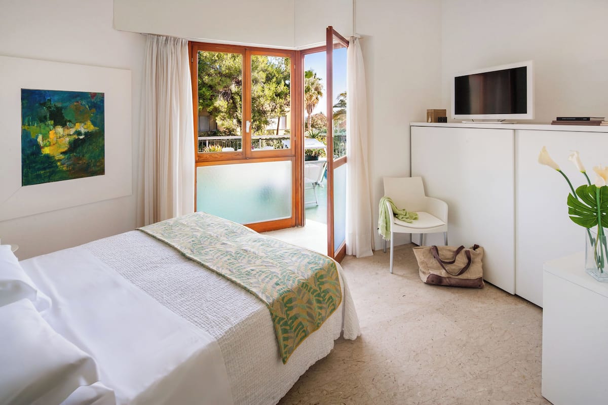 Quarto de hotel com cama, televisão, escrivaninha e vista para o exterior.