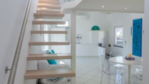 Interior moderno com escada para um segundo andar, área de jantar com cadeiras transparentes e cozinha com armários brancos.