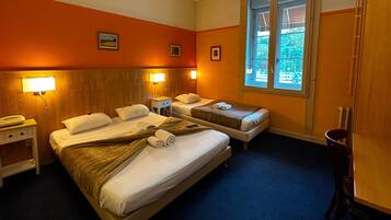 Quarto de hotel com duas camas, uma mesinha de cabeceira, uma luminária e uma janela com vista para o exterior.