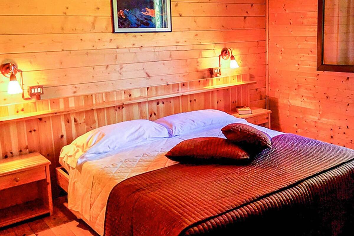 Quarto de cabana de madeira com cama, duas luminárias de cabeceira e um quadro na parede.