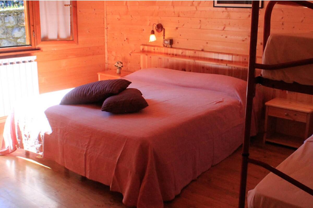 Quarto de madeira com cama, mesa de cabeceira, luminária e janela.