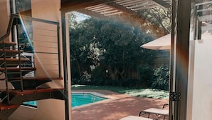 Uma casa moderna com porta de vidro que dá para um quintal com piscina, um pátio com cadeiras e uma escada de madeira.