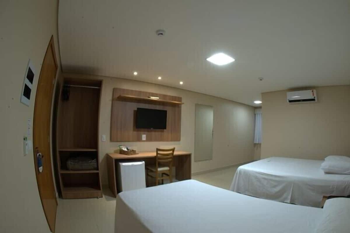 Quarto de hotel com duas camas, uma escrivaninha, uma televisão e um guarda-roupa.