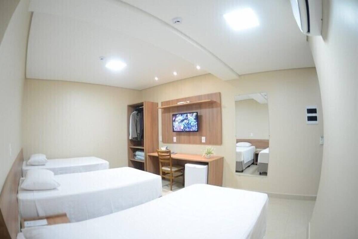 Quarto de hotel com duas camas, uma escrivaninha, televisão, guarda-roupa e espelho.