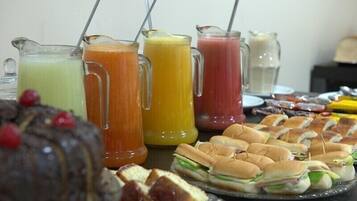 Uma mesa de buffet com diversos sanduíches e jarras de sucos de frutas.