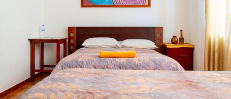 Quarto de hotel com uma cama grande, mesa de cabeceira, garrafa de água e um quadro na parede.