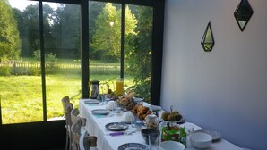 Mesa de jantar posta com pratos, copos e talheres, com vista para um gramado com árvores.
