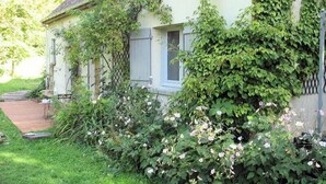 Uma casa com jardim, um deck de madeira e uma janela com persianas.