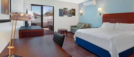 Quarto de hotel com cama, escrivaninha, cadeira, mesinha, sofá e varanda com vista.