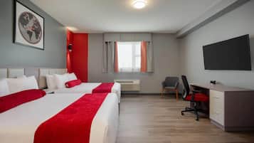Quarto de hotel com duas camas, uma escrivaninha, uma cadeira, televisão de tela plana e uma janela com cortinas.