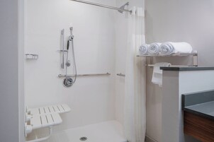 Chuveiro com chuveiro manual, box de vidro e porta-toalhas com toalhas.