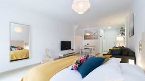 Quarto moderno com uma cama grande, televisão, área de refeições e espaço de estar.