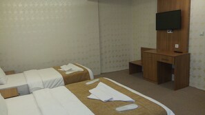 Quarto de hotel com duas camas, uma escrivaninha, uma televisão e um banquinho.
