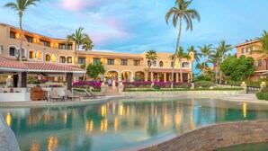 Um resort com piscina, palmeiras e um edifício com várias varandas.