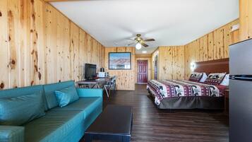 Quarto com decoração em madeira, uma cama com roupa de cama estampada, um sofá, uma escrivaninha com um computador e um ventilador de teto.