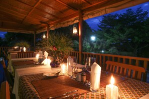 Uma área de refeições ao ar livre com mesas preparadas para dois, velas e vista para o céu noturno.