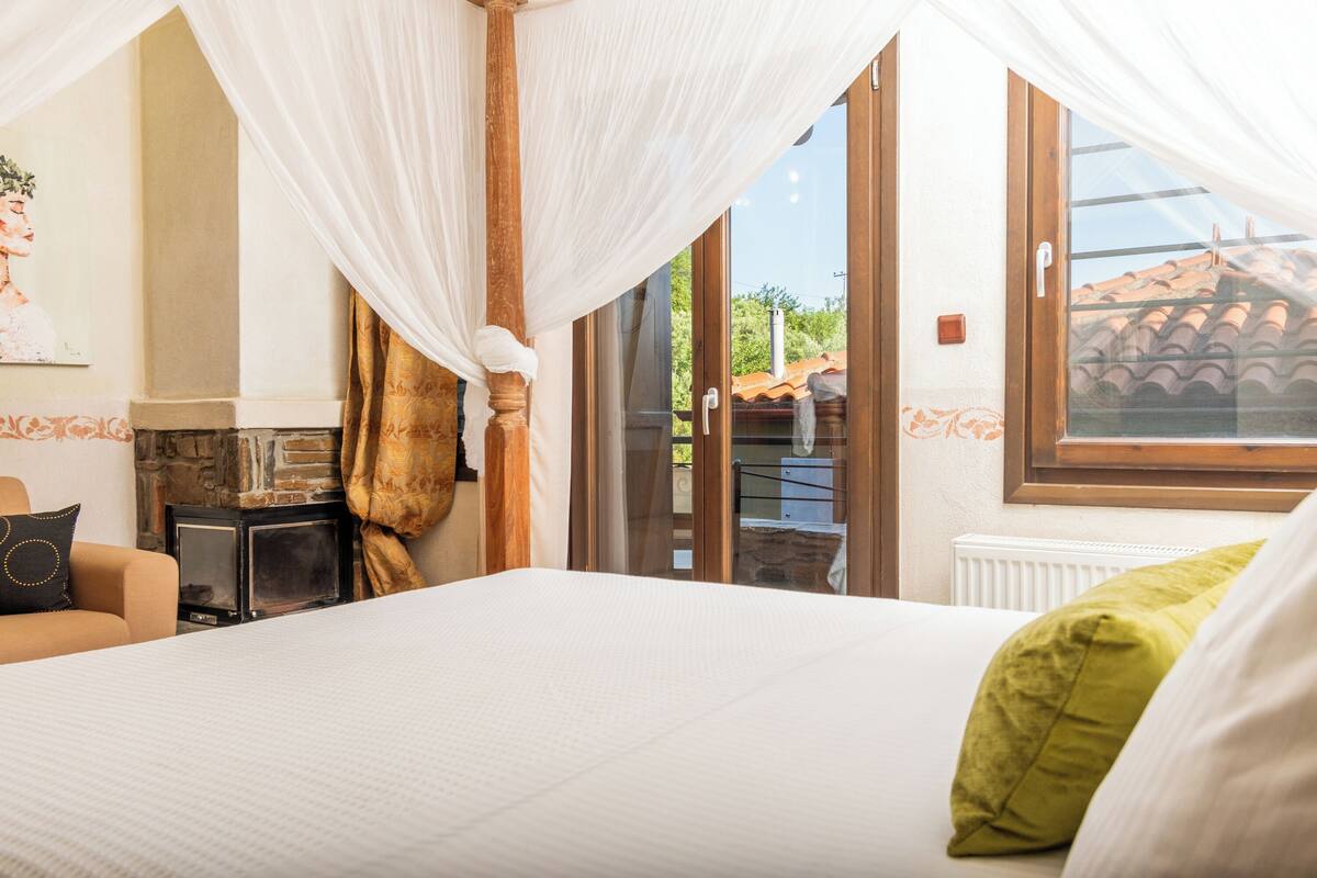 Quarto com cama de dossel, lareira e vista para o exterior.