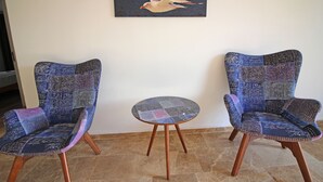 Duas poltronas estofadas com design de retalhos, uma mesinha redonda e um quadro de gaivota na parede.