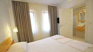 Quarto de hotel com uma cama grande, luminária de cabeceira e banheiro com pia e espelho.