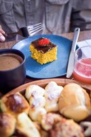 Um prato de sobremesa com uma fatia de bolo coberta com uma morango, uma xícara de café e um copo de bebida vermelha.