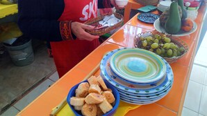 Uma bancada de cozinha com uma pessoa de avental vermelho segurando uma tigela, uma pilha de pratos e uma cesta de uvas.