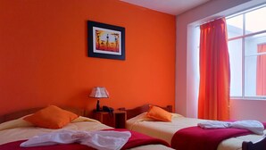 Quarto de hotel com duas camas, paredes laranja, um quadro na parede, uma luminária e uma janela com cortinas.