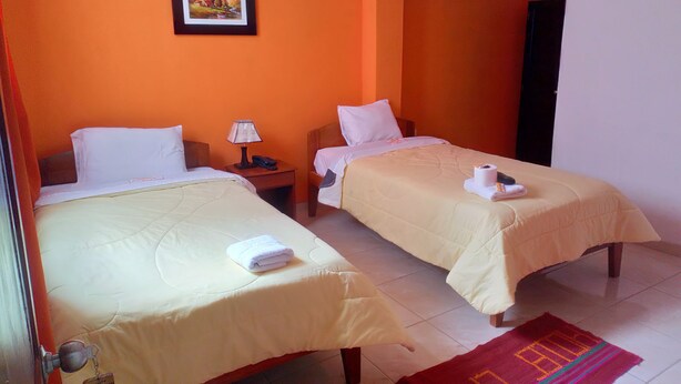 Quarto de hotel com duas camas, mesa de cabeceira, abajur e um quadro na parede.