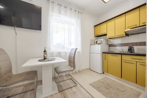 Uma cozinha compacta com armários amarelos, bancada branca e um espaço de refeições com mesa e cadeiras.