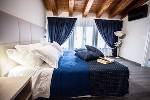 Quarto com cama, mesa de cabeceira, televisão na parede e janela com cortinas.