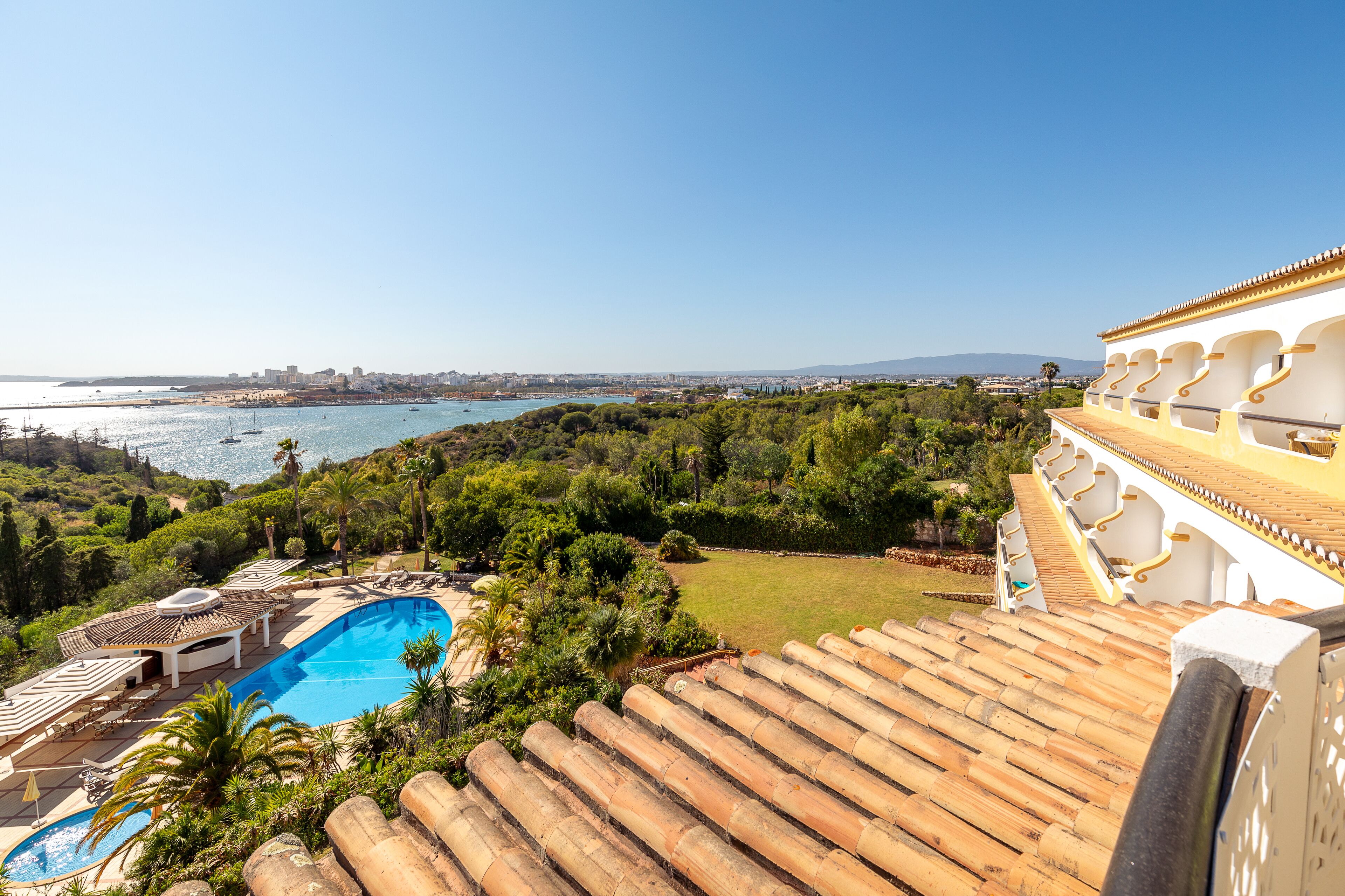 Área de piscina no terraço com vista para o mar e para a paisagem urbana.
