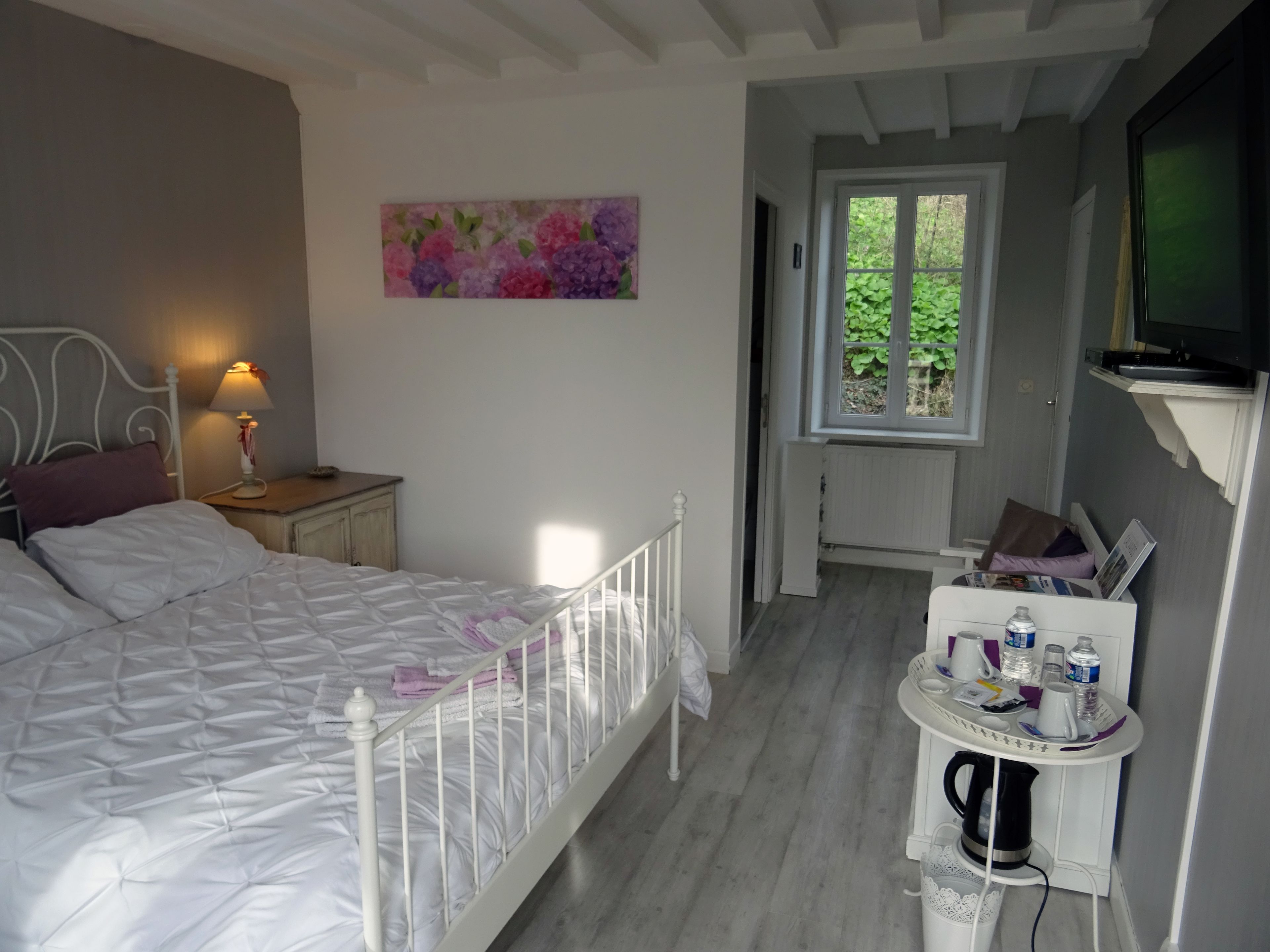 Quarto com cama, luminária de cabeceira e janela com vista para o verde.