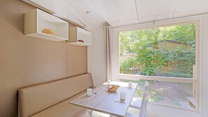 Quarto com um banco, uma mesa e uma janela com vista para o verde.