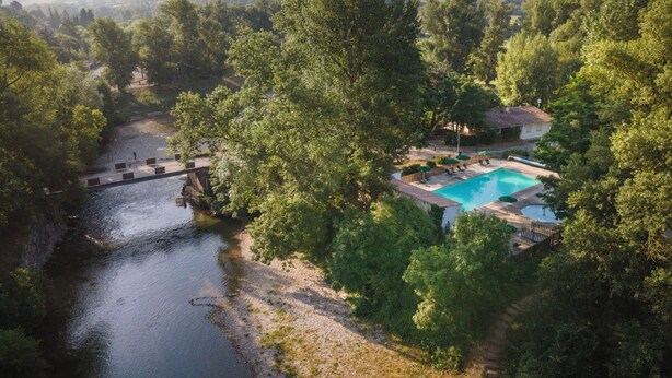 Uma propriedade à beira do rio com piscina, uma ponte e paisagem arborizada.