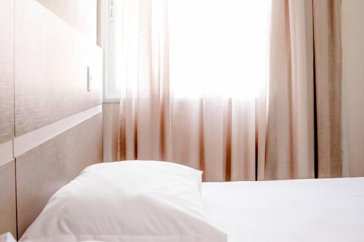 Quarto de hotel com cama, janela com cortinas e cabeceira.