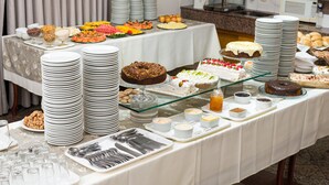 Uma mesa de buffet com diversos alimentos e pratos empilhados.