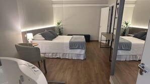 Quarto de hotel moderno com duas camas, área de estar com uma cadeira, uma mesinha e uma banheira grande.