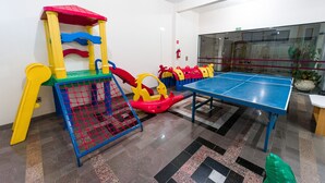 Espaço infantil com estrutura de escalada, pequeno escorregador e mesa de pingue-pongue.