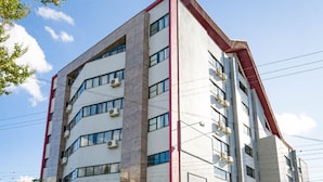 Um hotel de vários andares com design moderno, com uma entrada destacada e vários carros estacionados na frente.