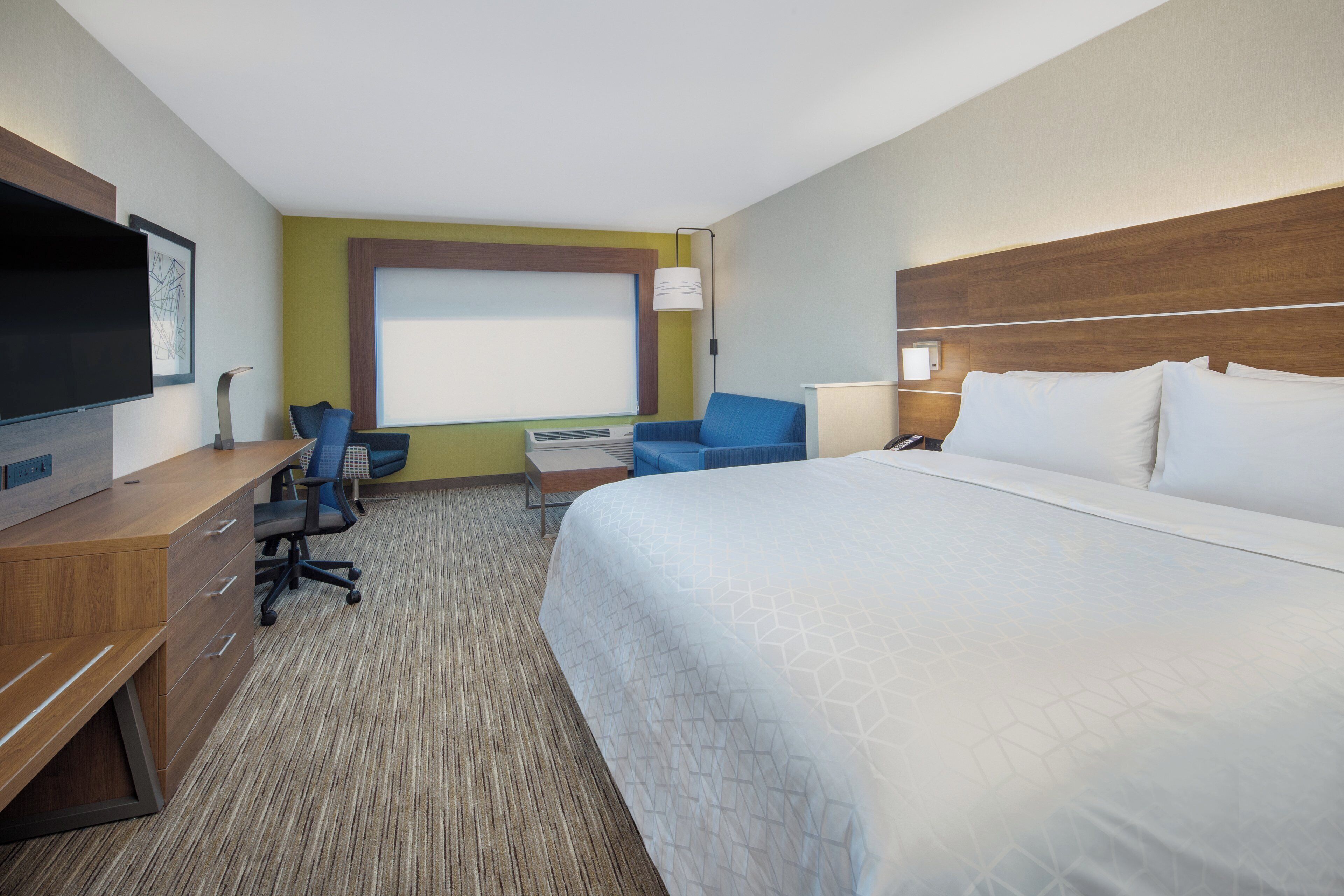 Quarto de hotel com uma cama grande, uma escrivaninha com cadeira, televisão e janela com persianas.